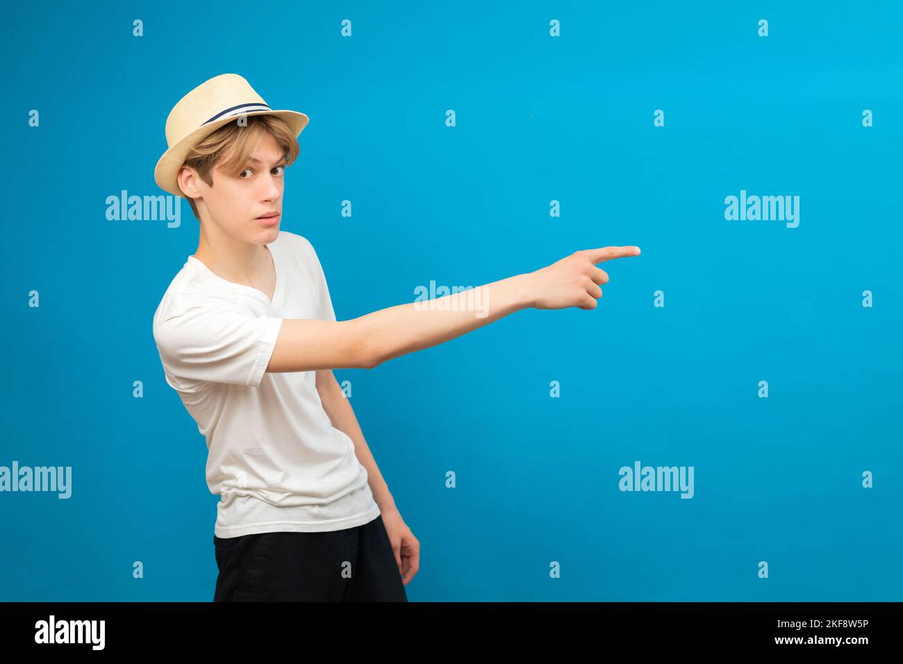 Young teen man points palms aside isolated on blue. Friendly well ...