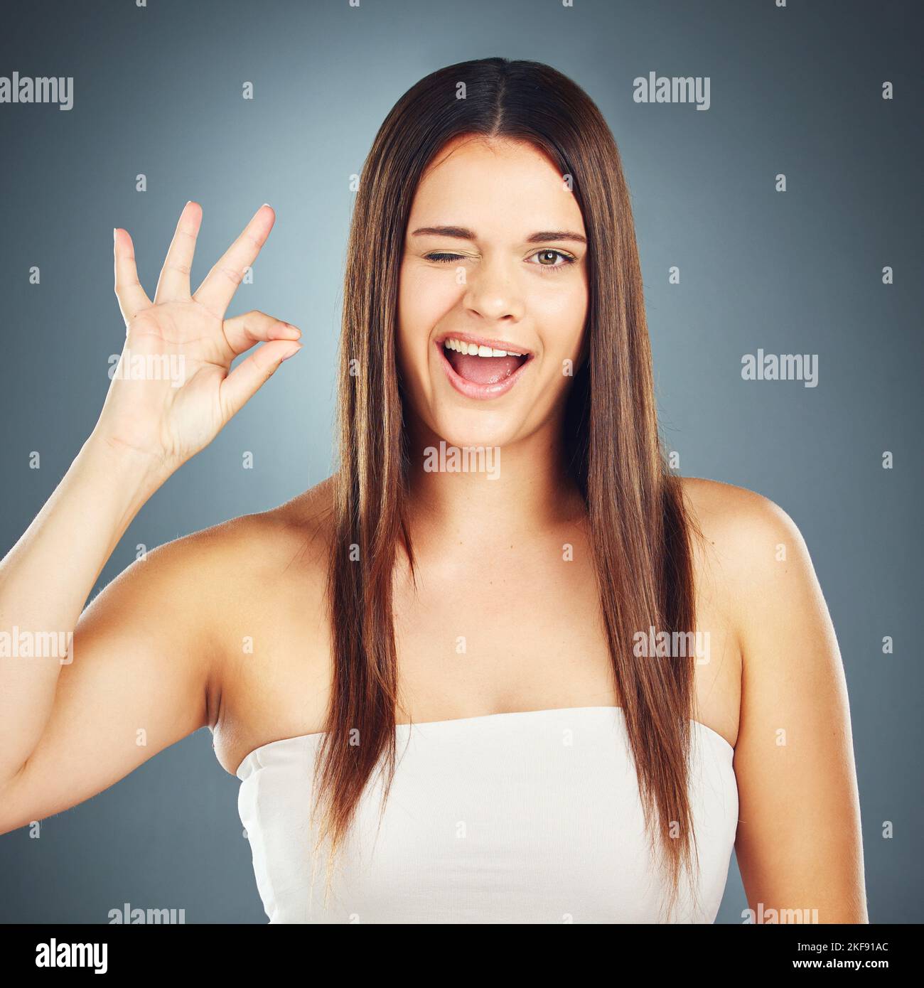 Hand sign, perfect and wink with a model woman in studio on a blue ...