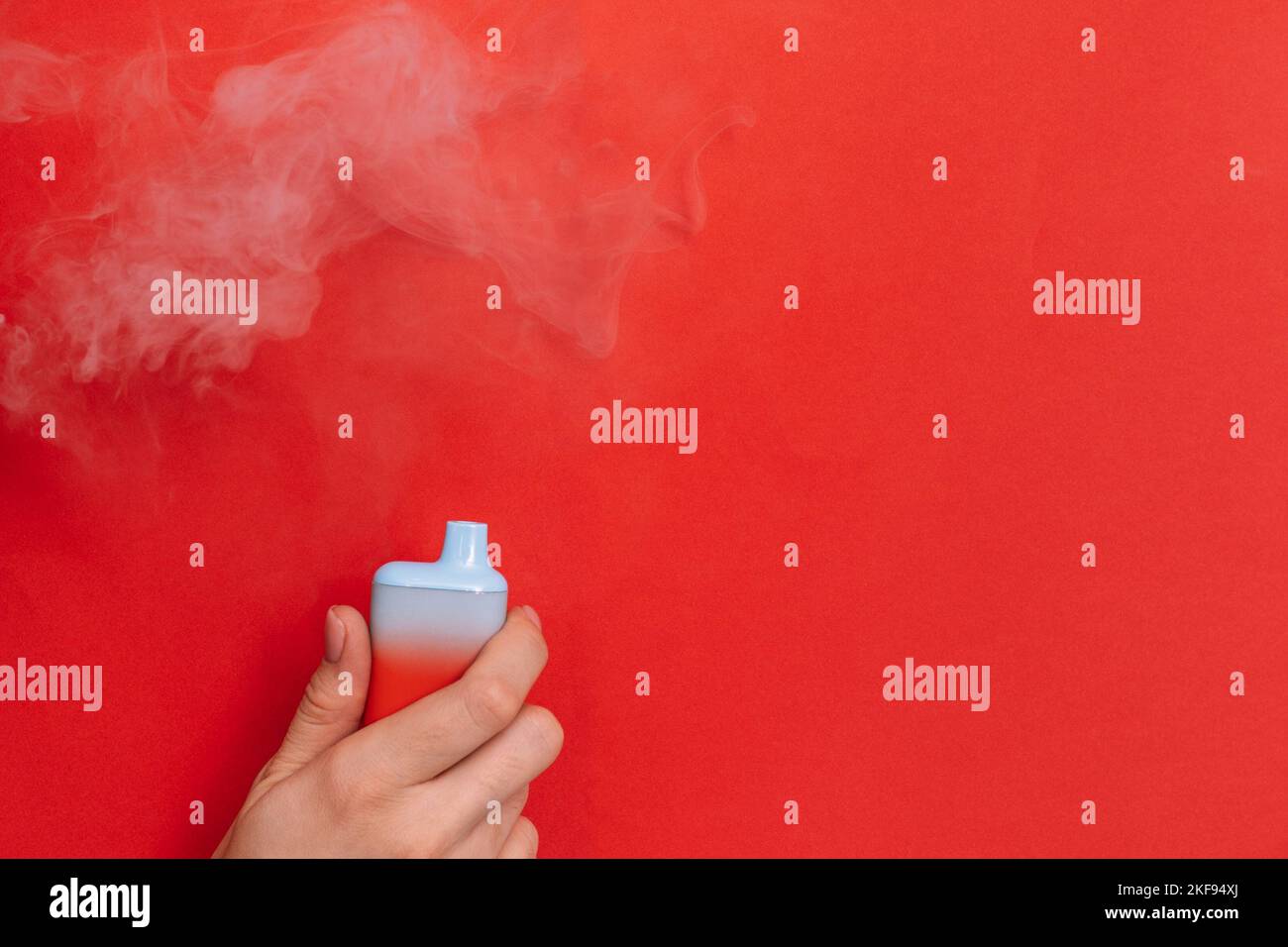 Exhalation of smoke from vape in female hand against red background ...