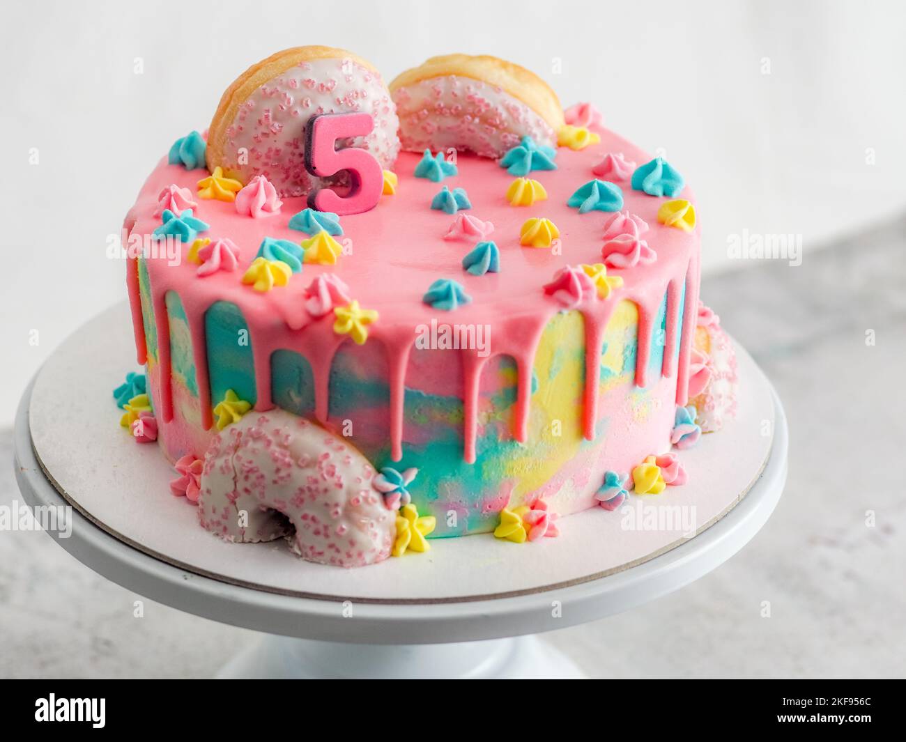 Close up of pink frosted dripping cake with donut and plastel brushed ...