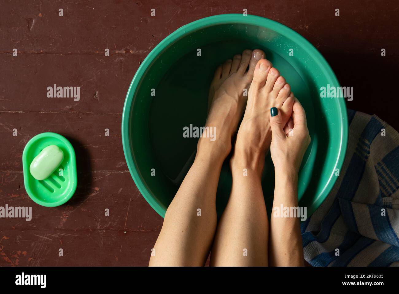 Girl Washes Her Feet In A Green Bowl On The Wooden Floor Of The House