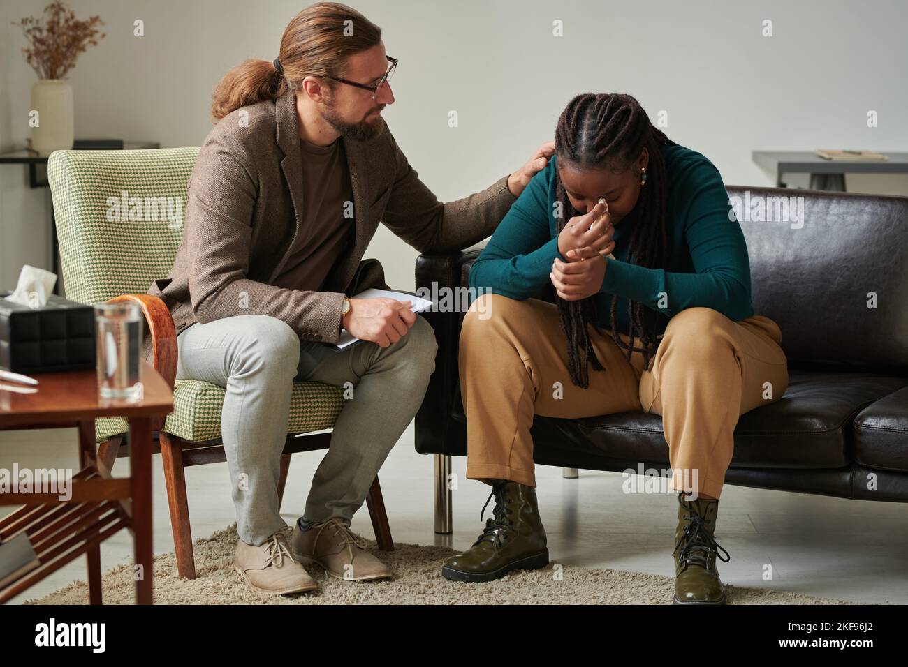 Psychologist supporting patient while she crying sitting on sofa during ...