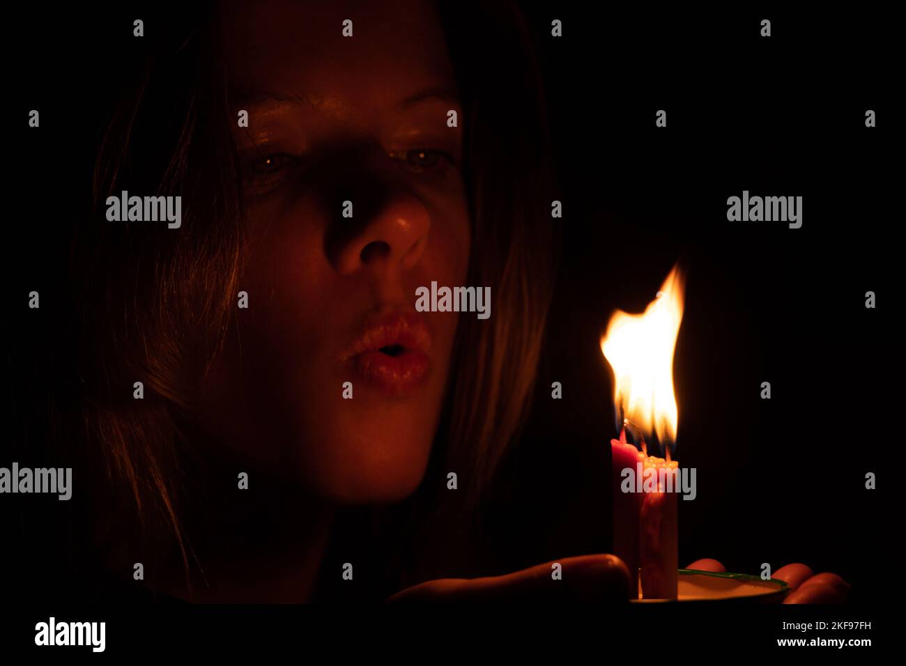 portrait of a young girl against the background of burning candles in the dark, candle flame in ...