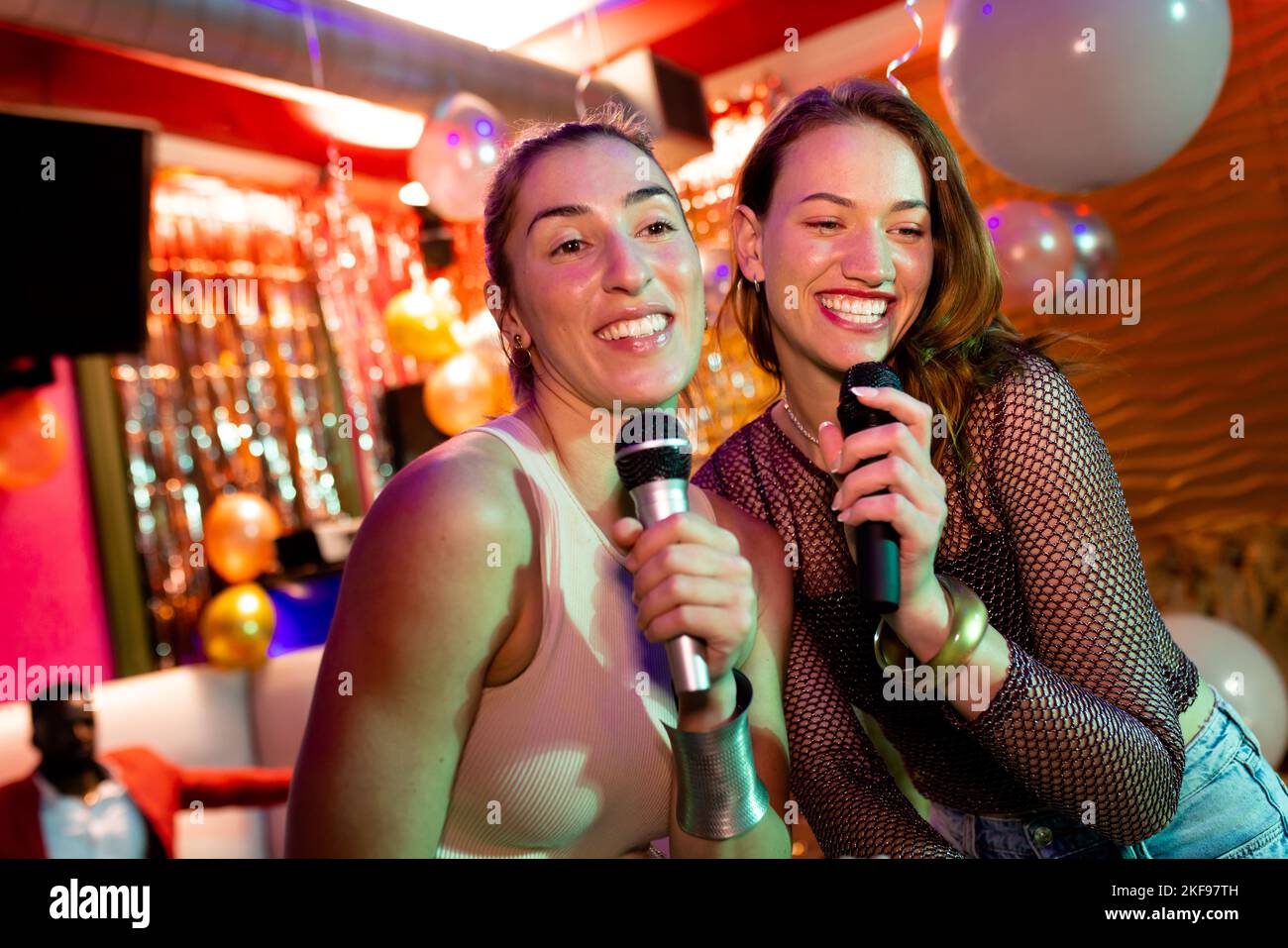 Two happy caucasian female friends singing karaoke at a nightclub bar ...