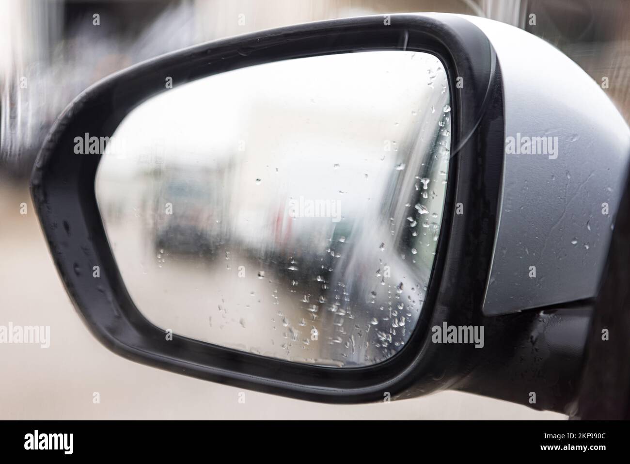Rearview mirror with raindrops and blurred background, in a gray ...