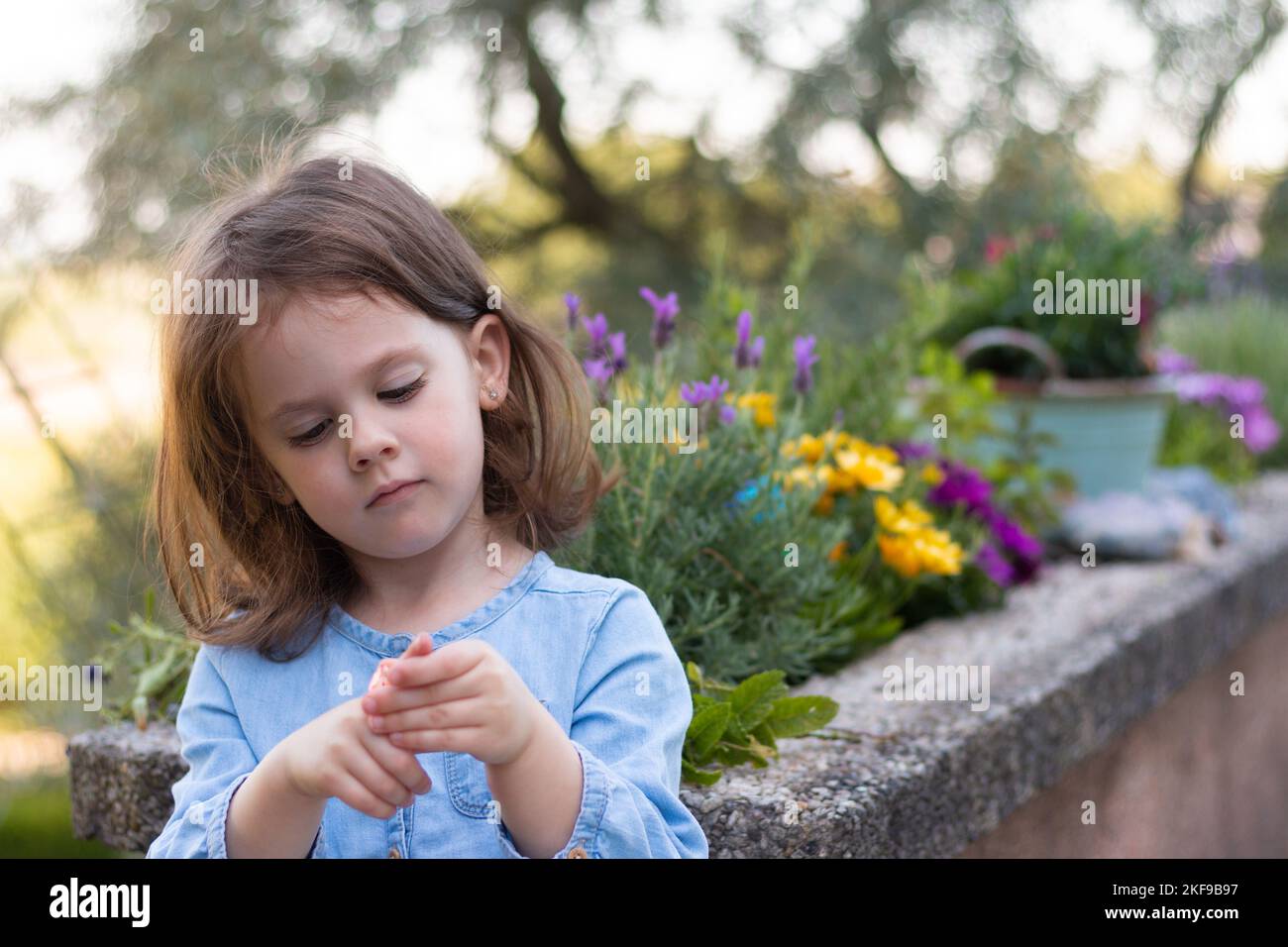 A little beautiful preschooler girl in a denim dress stands on a ...