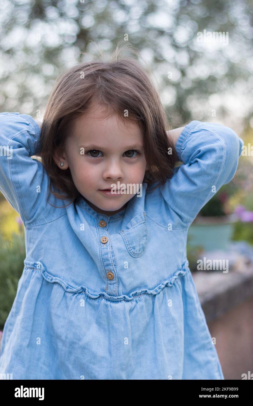 A little beautiful preschooler girl stands in a denim blue dress ...