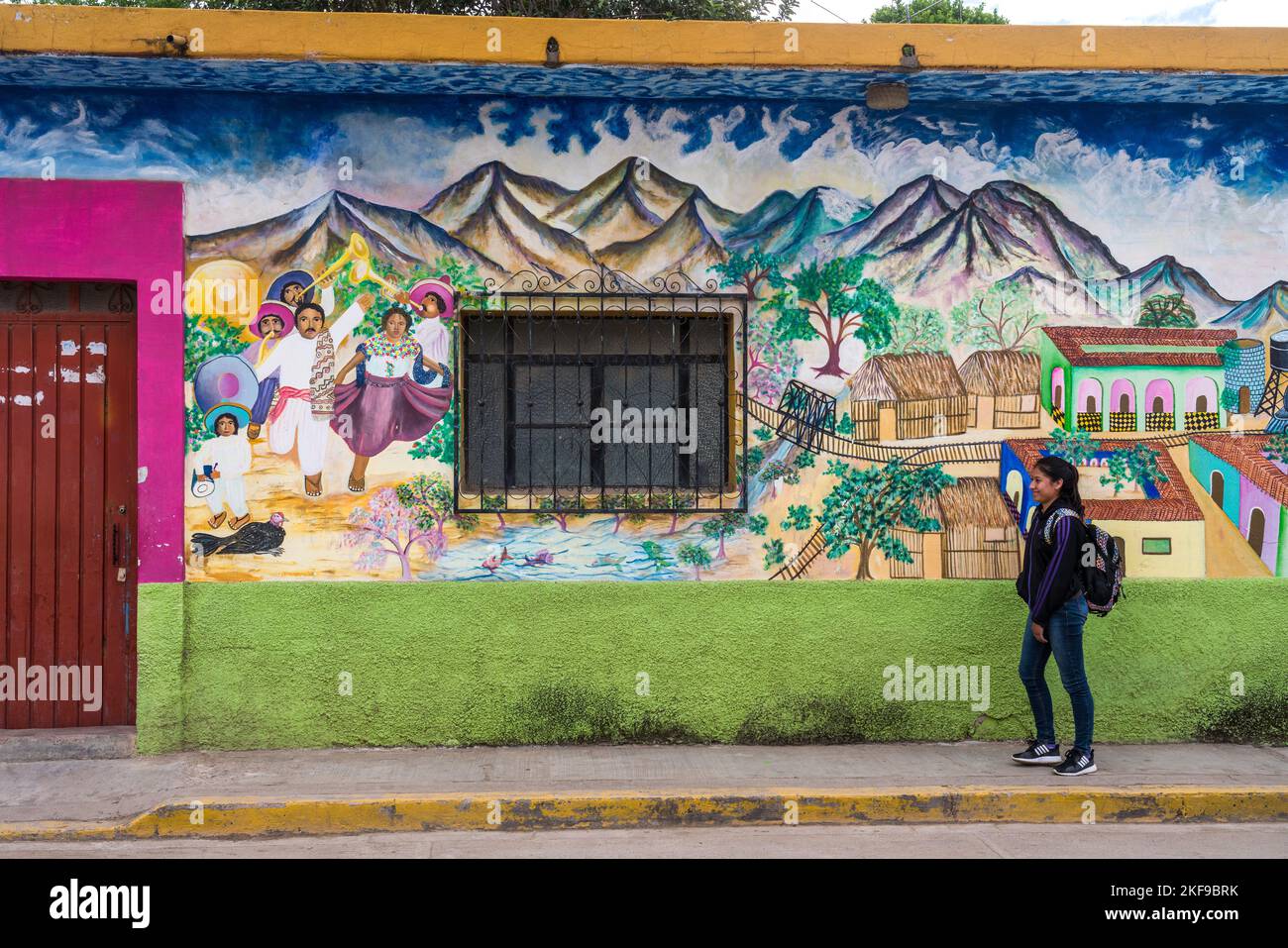 A young girlw walks by a painted mural depicting village life on the ...