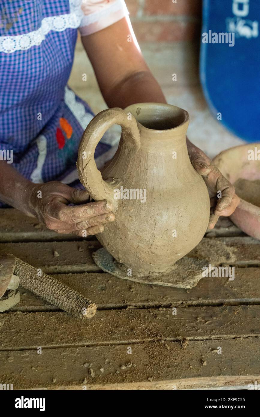 Making red clay pottery. The potter attaches a handle to make a pitcher ...