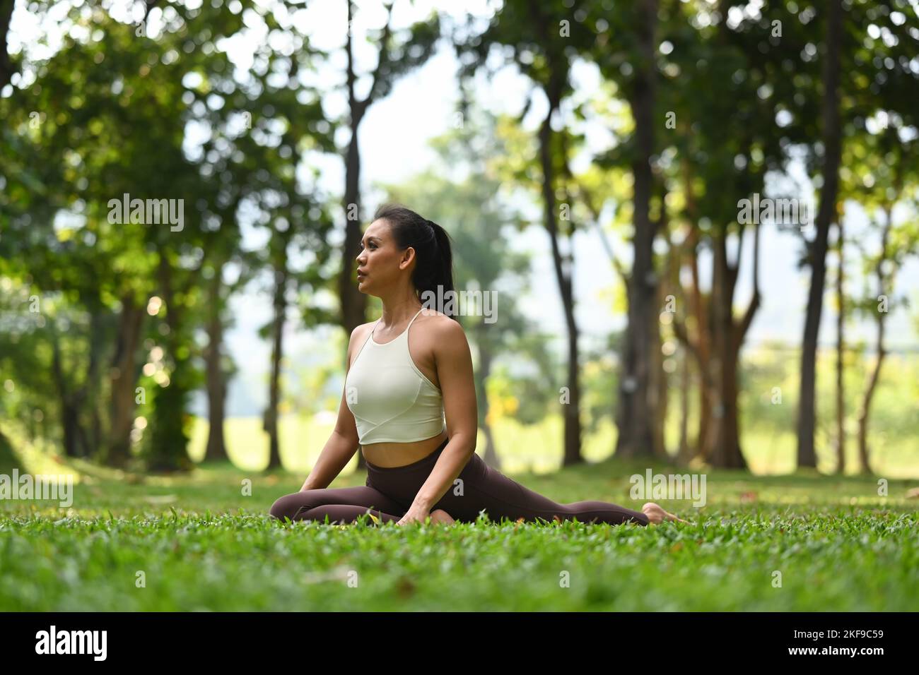 Gorgeous sporty woman practicing yoga in Half pigeon pose at green park ...