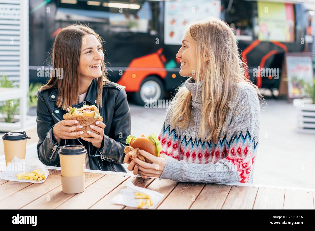 Two middle-aged women eat fast food and chat at a street food market ...
