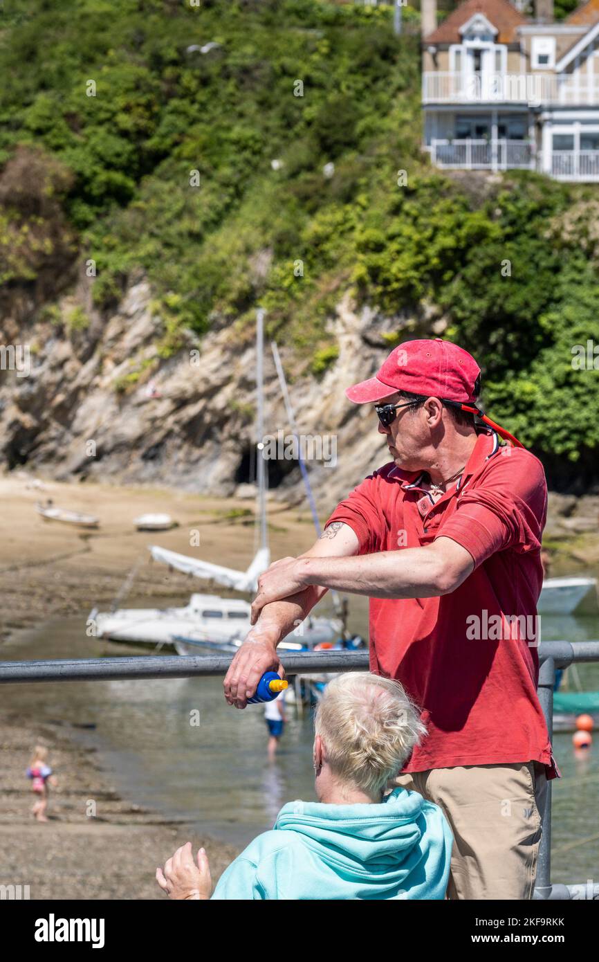 A male holidaymaker applying sun screen cream under intense sunshine in ...