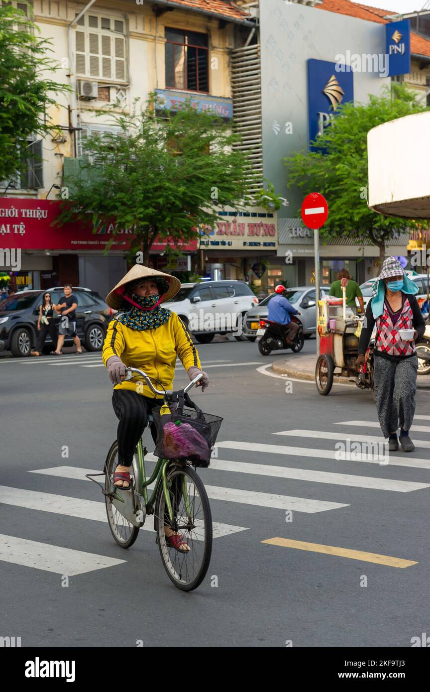 A cyclist wearing a conical hat passes by the Ben Thanh market, Ho Chi ...