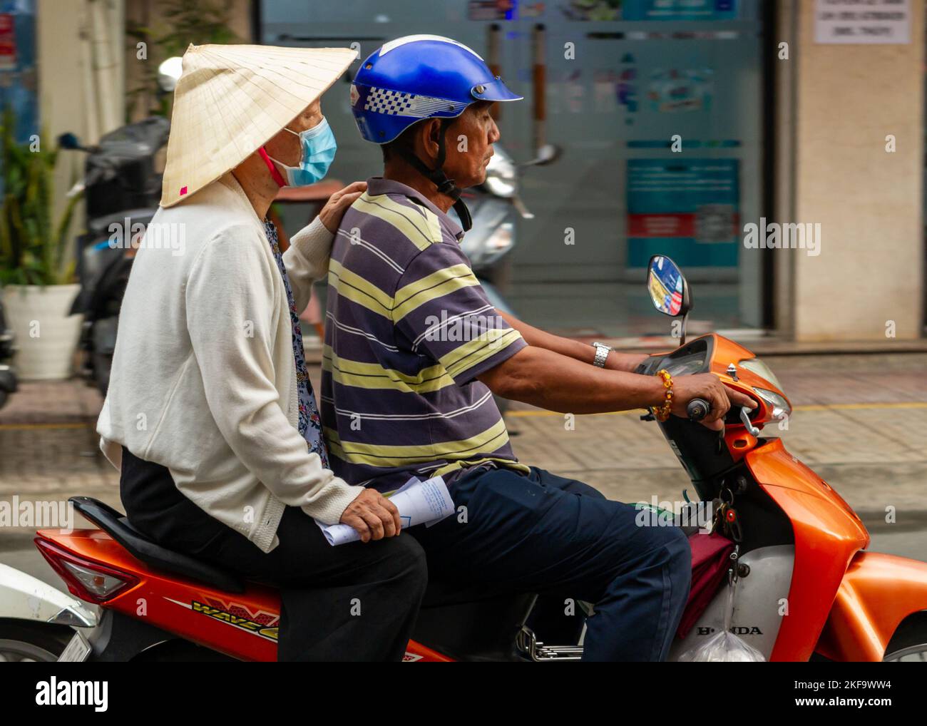 Saigon Street Life. A lady wearing a conical hat rides a motorcycle ...