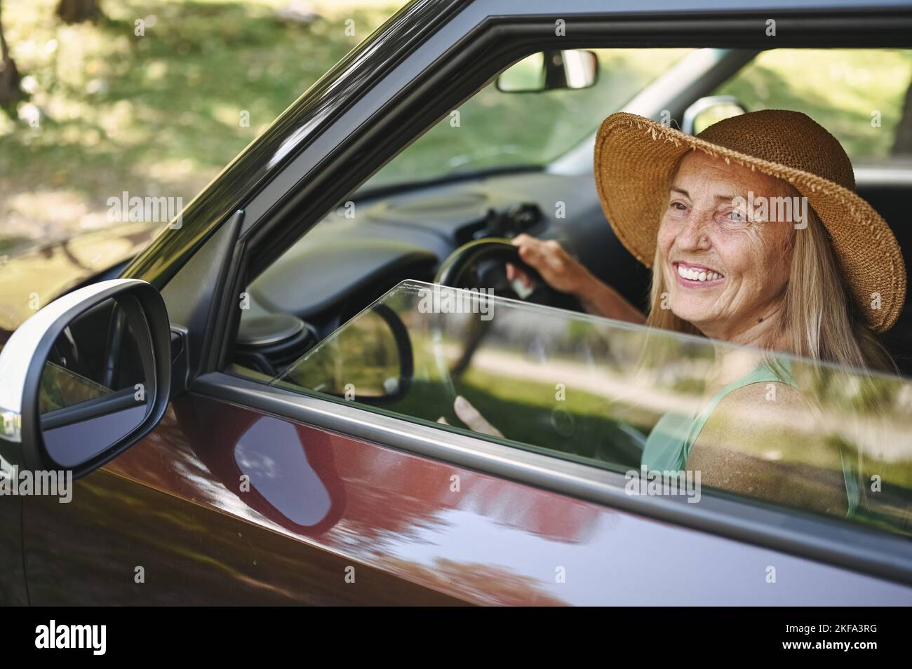 Happy senior woman driver in straw hat driving sitting in new car ...