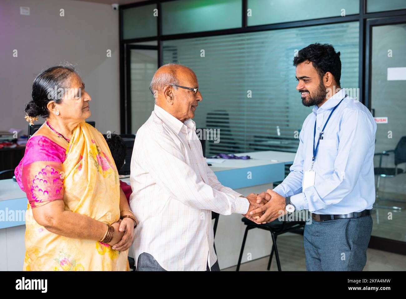 Happy smiling banker greeting by shaking hand of elderly couple at bank ...