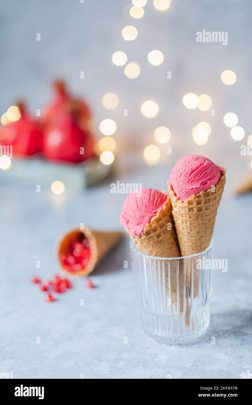 Healthy creamy pomegranate ice cream in a waffle cone on a gray table ...