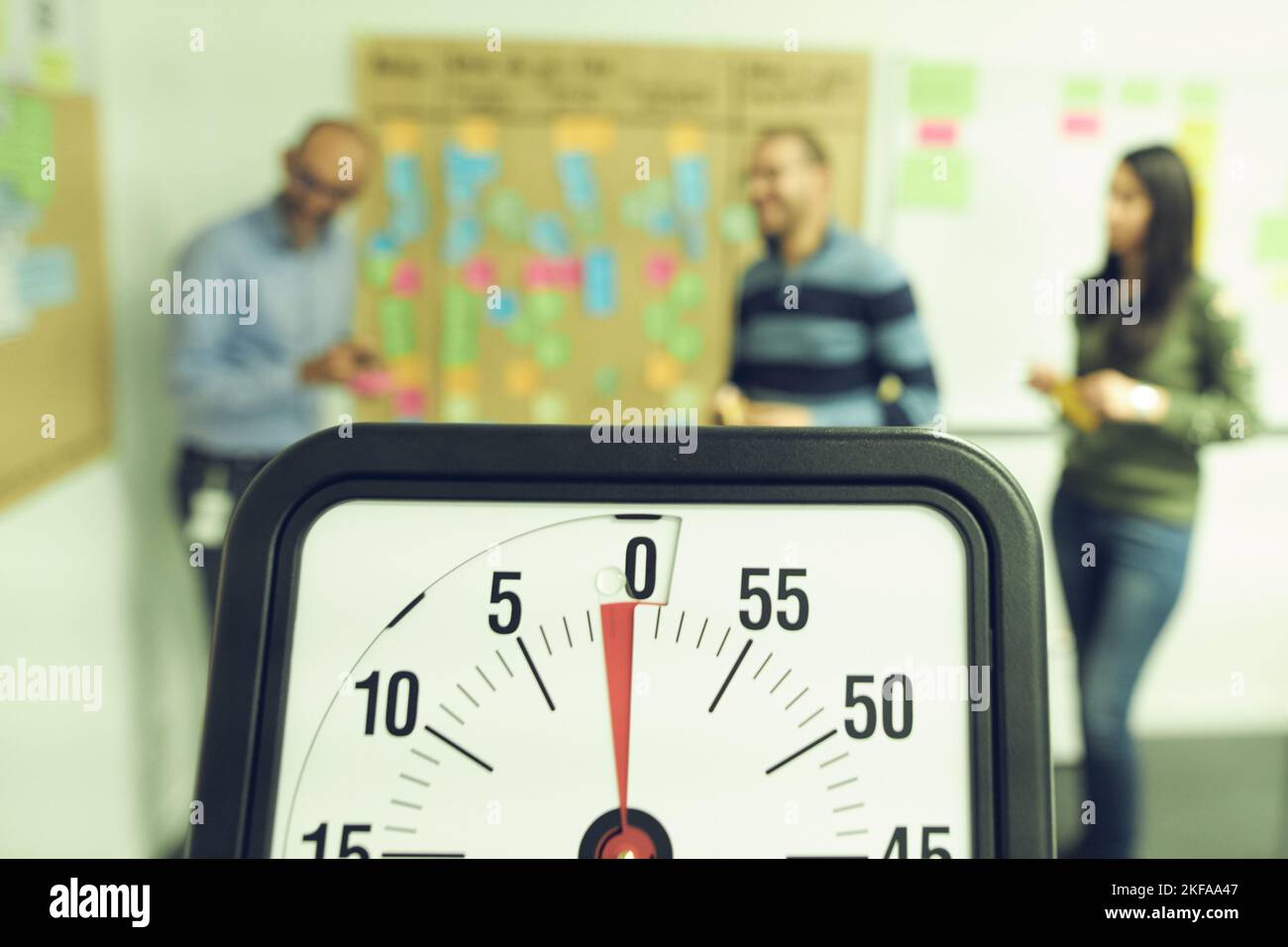 A closeup of a timer with a group of coworkers playing a game in the ...