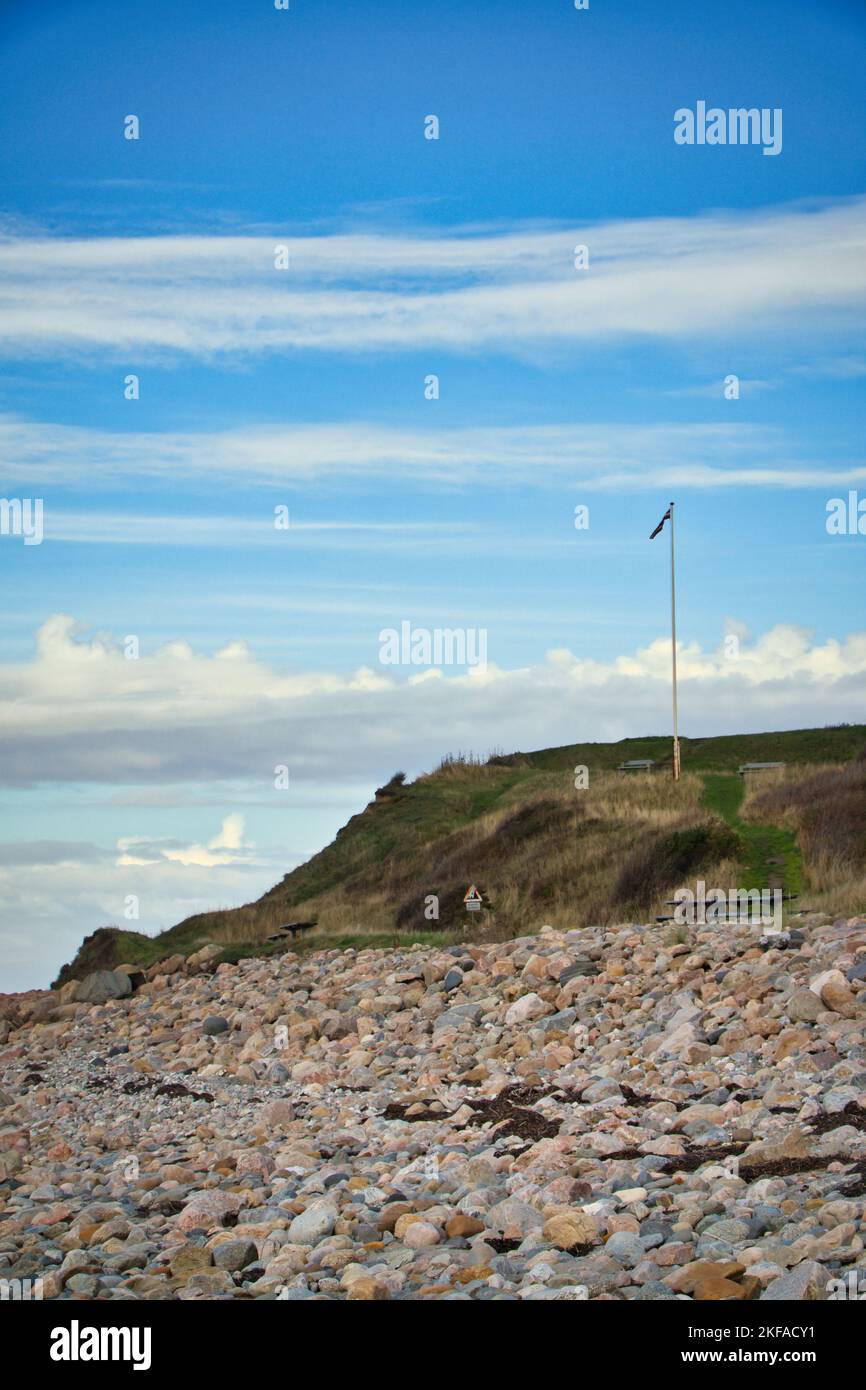 Stone beach by the sea. Flagpole with Danish flag on a hill. Danish ...
