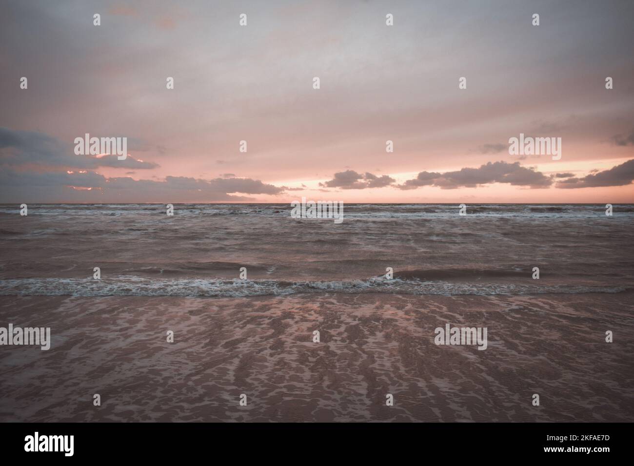 A scenic view of the sandy coast of the North Sea at sunset in cloudy ...