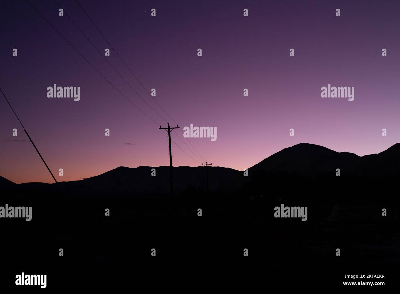 A purple starry sky over a silhouette of a mountain and a electricity ...
