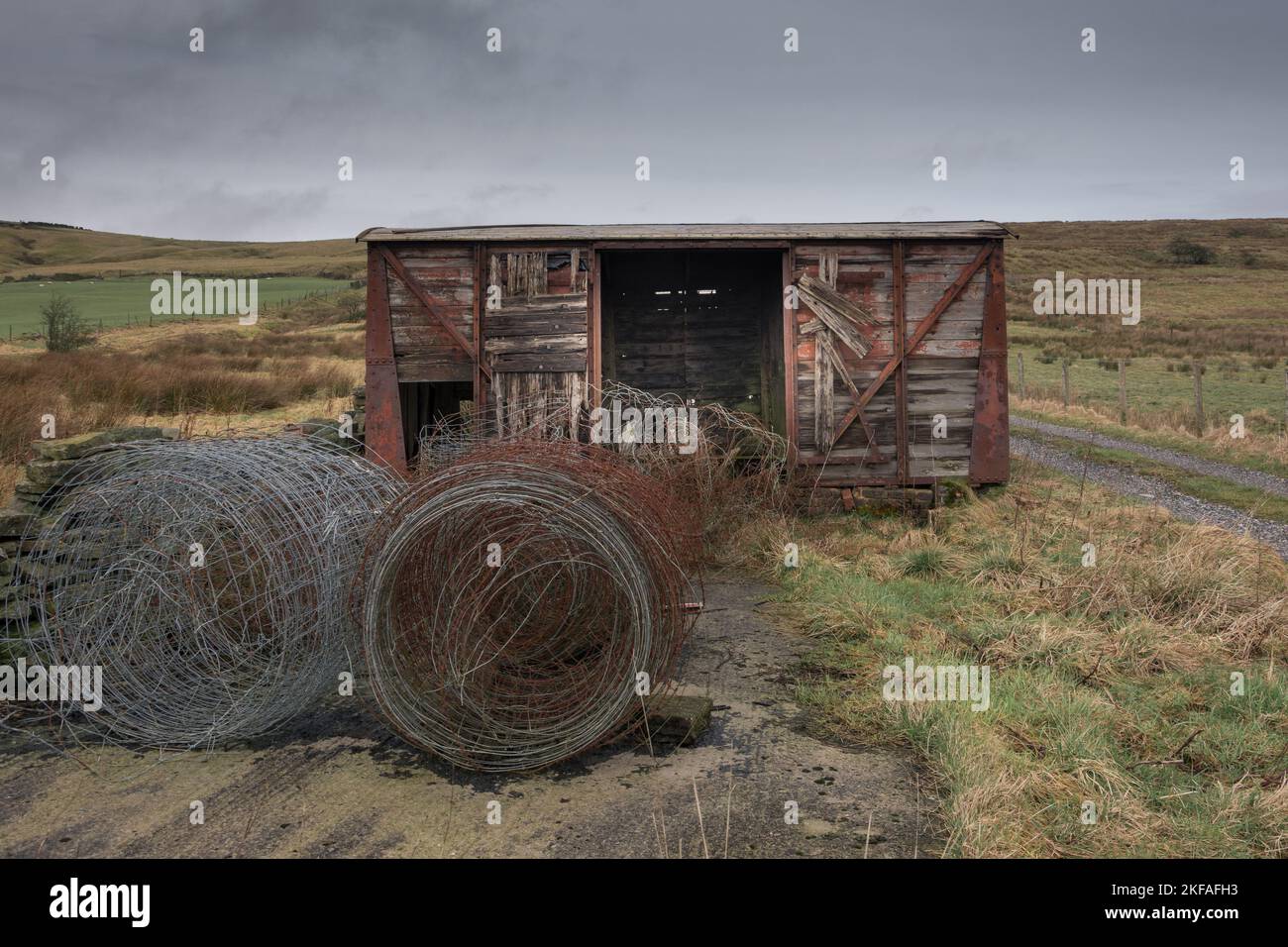 Derelict old red rustic wooden railway carriage with rolls of mesh ...