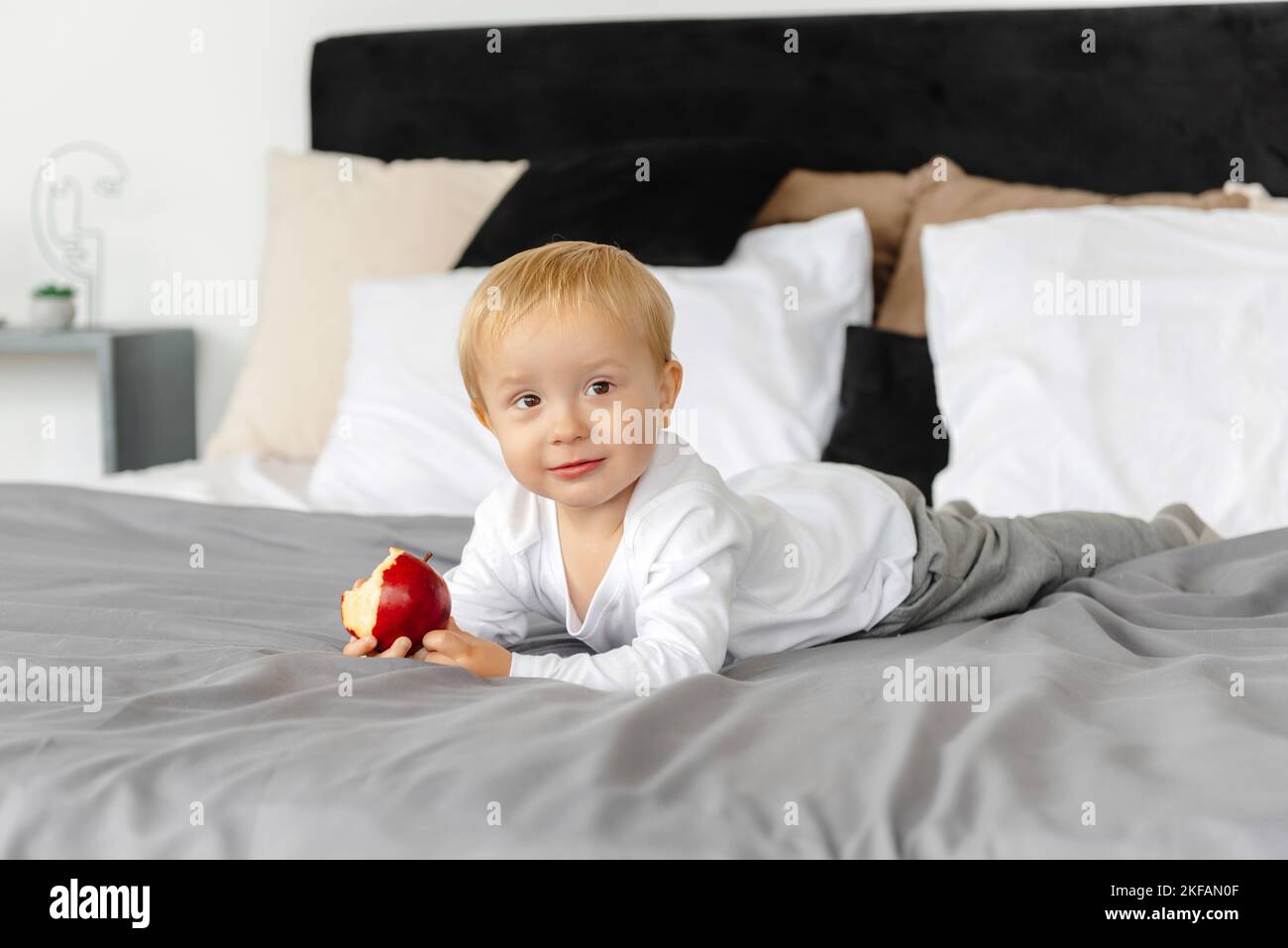 A cute, healthy baby is lying on the bed. The baby is holding and ...
