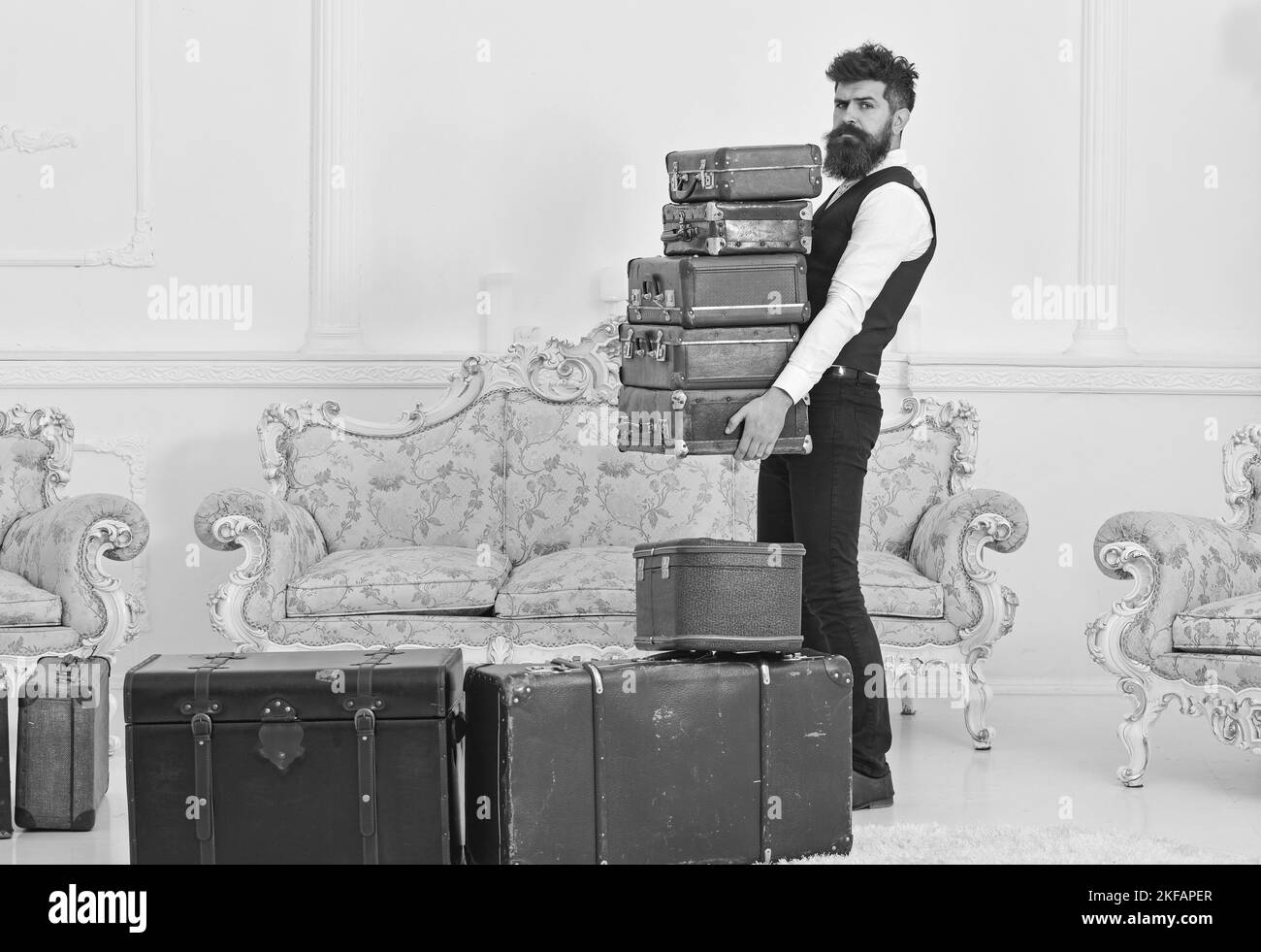 Macho, elegant porter on strict face carries pile of vintage suitcases ...