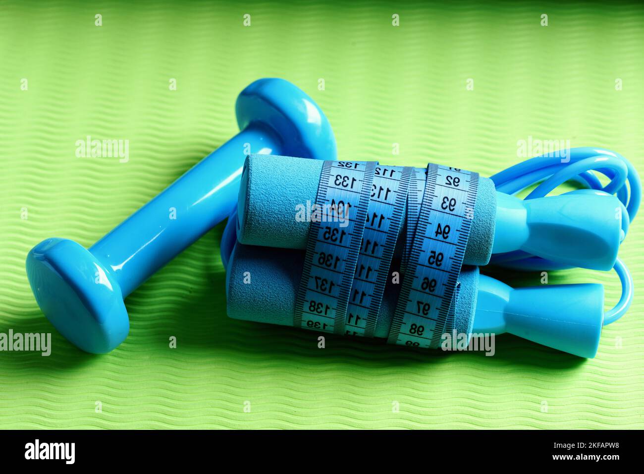 Measuring tape around jump rope and barbells on yoga mat Stock Photo ...