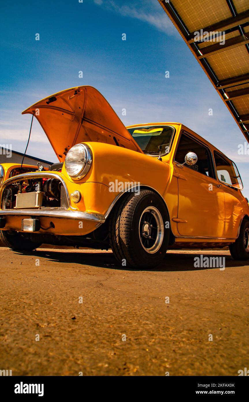 A vertical shot of a vintage yellow mini Cooper with the front popped ...