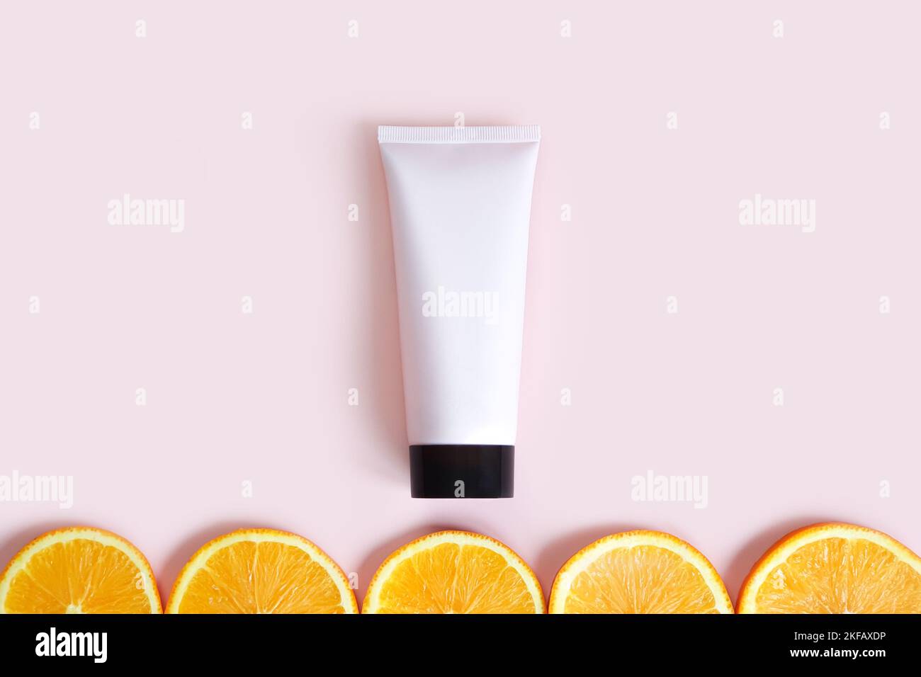 Pink squeeze bottle cream tube with black cap and orange slices on pink ...