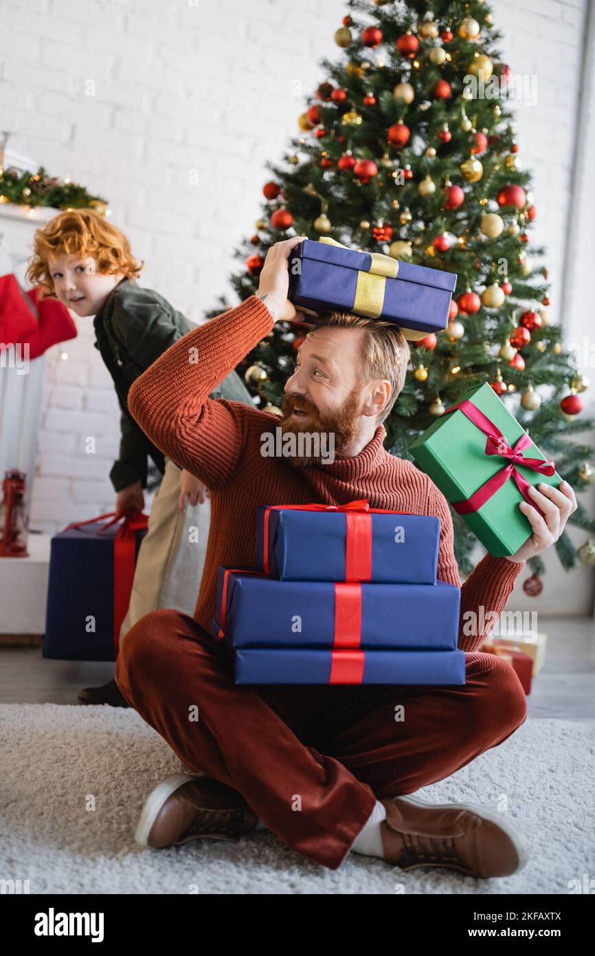 cheerful bearded man having fun with gift boxes near son and Christmas ...