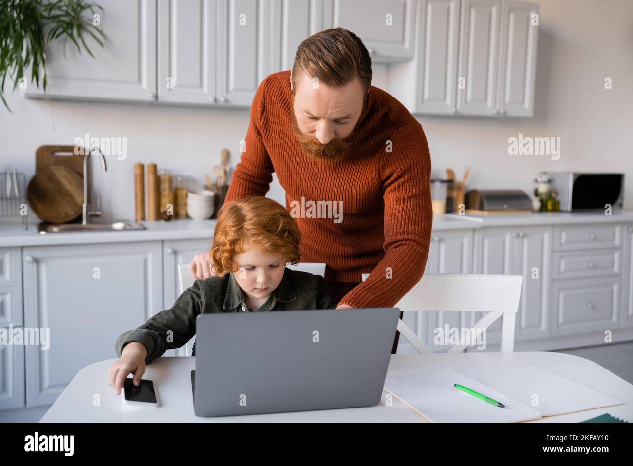 bearded man explaining something to redhead son doing homework near ...