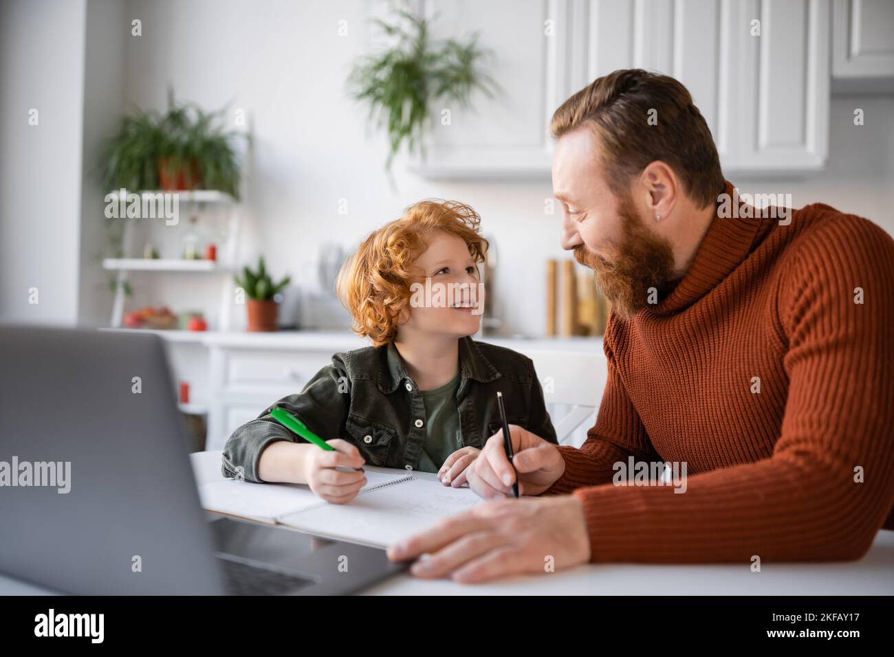bearded man helping smiling redhead son doing homework near blurred ...