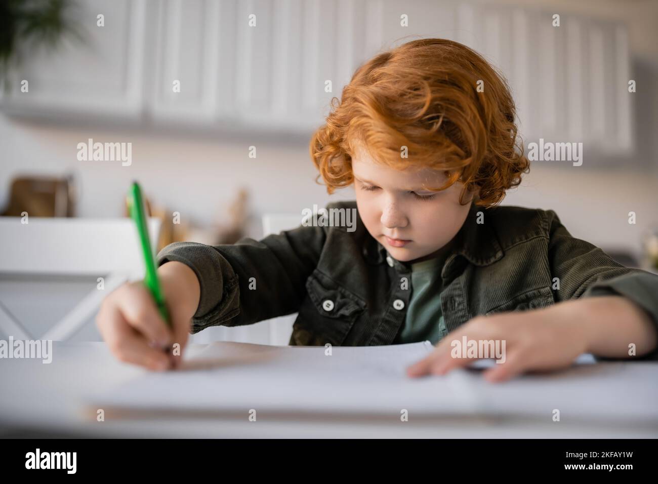 focused boy with red hair doing homework and writing in blurred ...