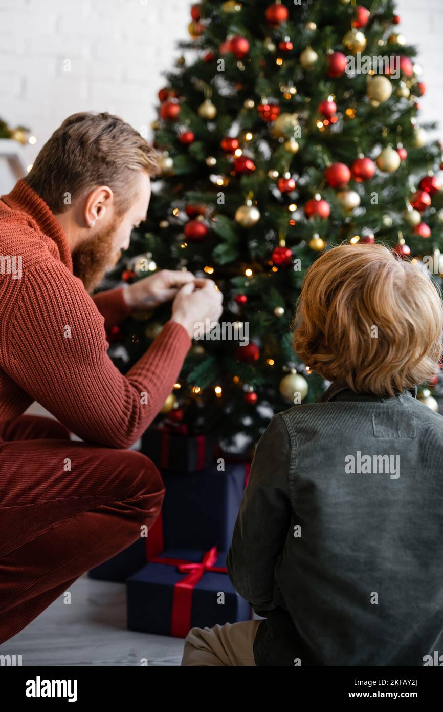 back view of redhead dad and son decorating blurred Christmas tree at ...