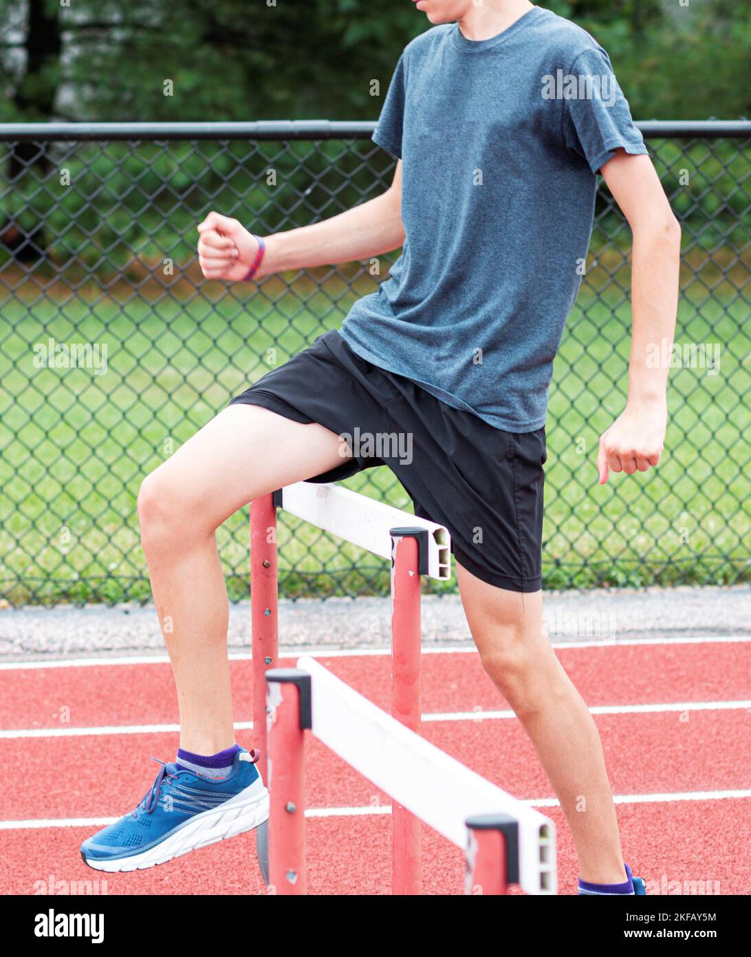 A high school track runner walking over track hurdles during practice ...