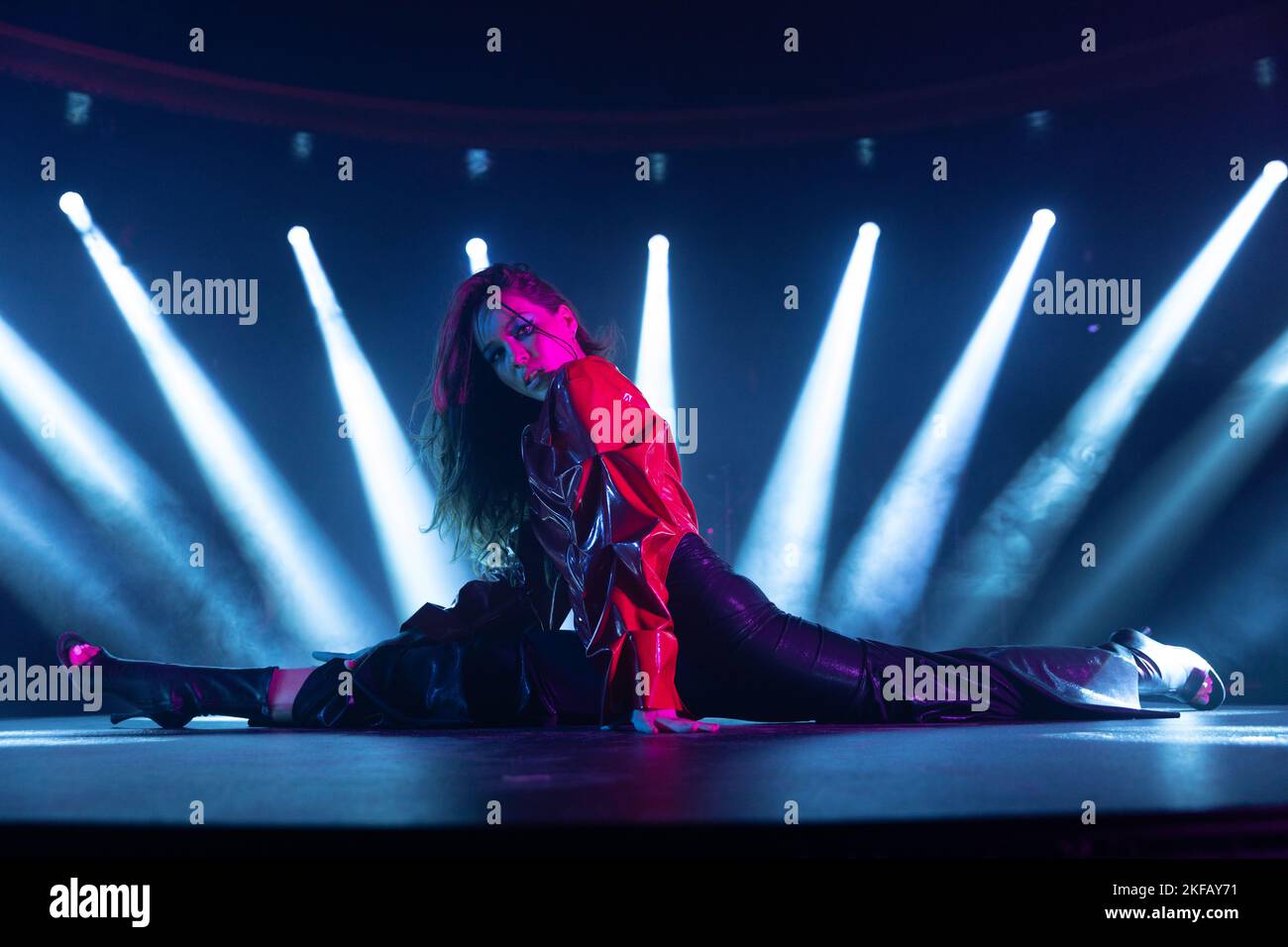 A young cool female performer doing a split on an illuminated stage ...
