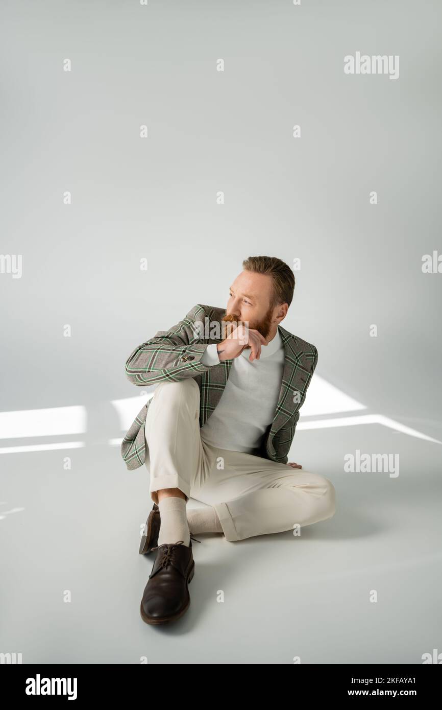 Bearded man in plaid jacket looking away while sitting on grey ...