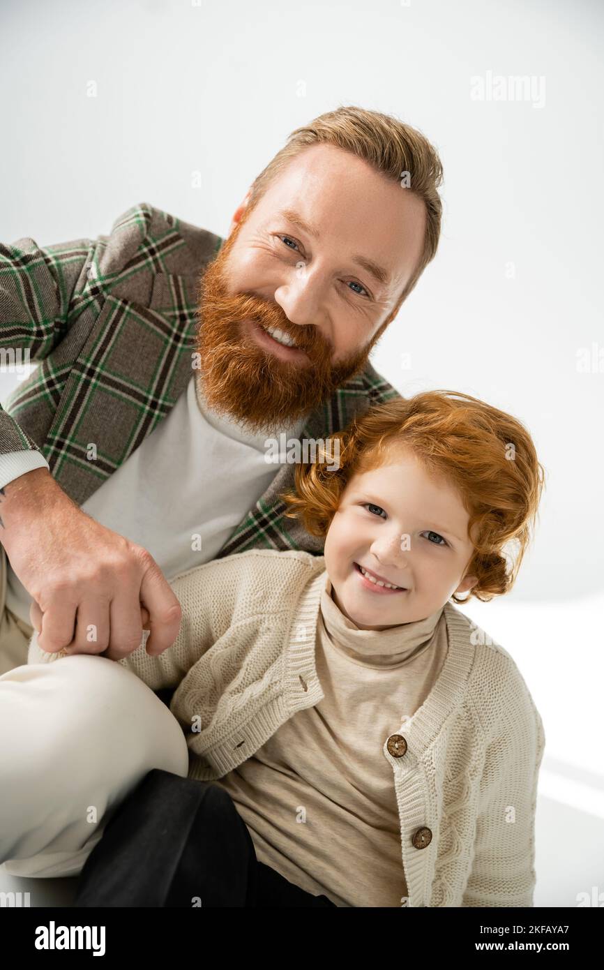 Portrait of trendy father and redhead boy smiling at camera on grey ...