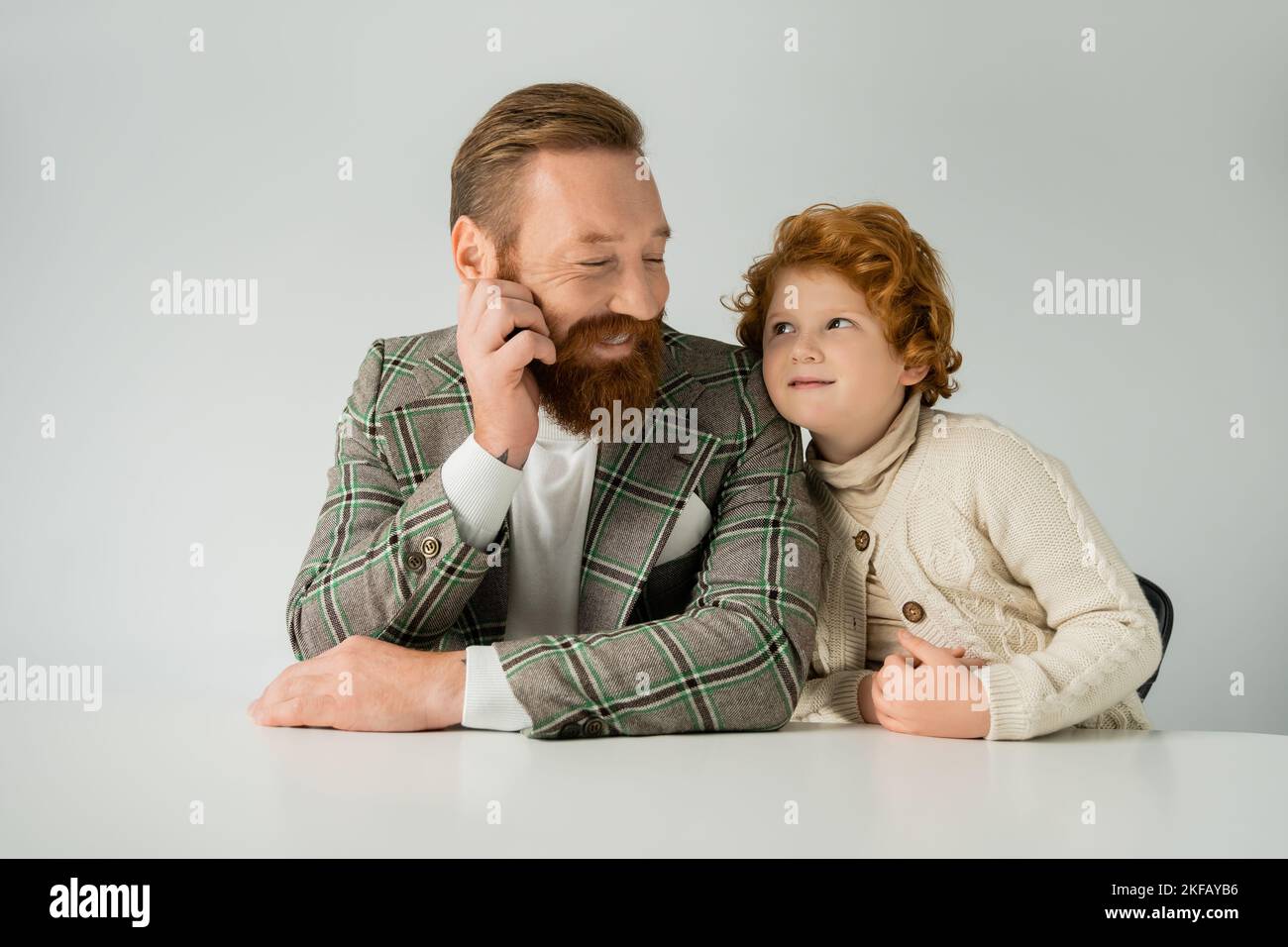 Redhead boy in jumper looking at positive dad isolated on grey Stock ...