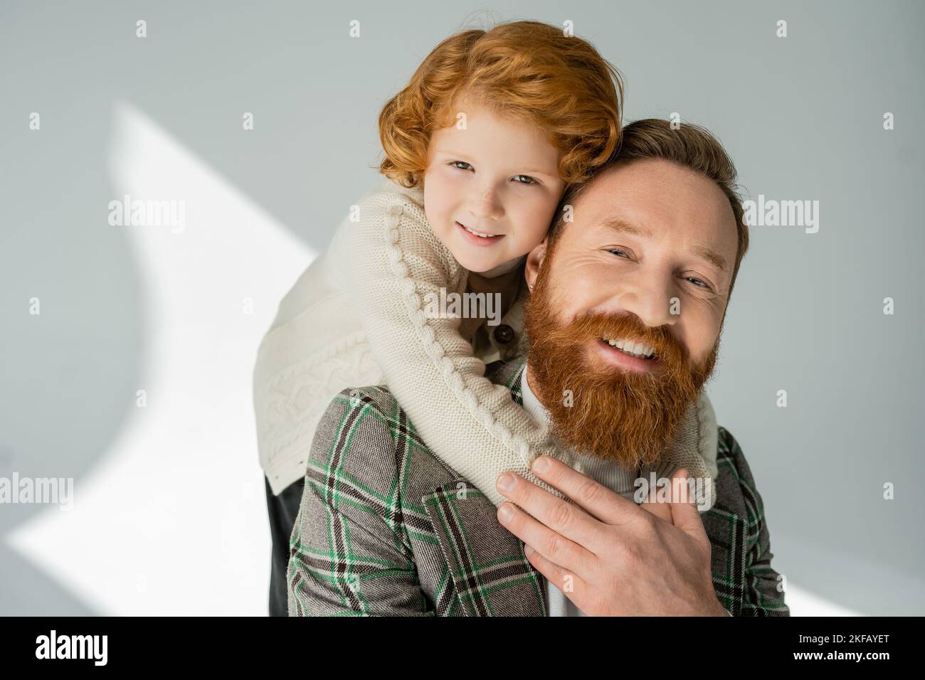 Redhead son in warm jumper looking at camera while embracing dad on ...
