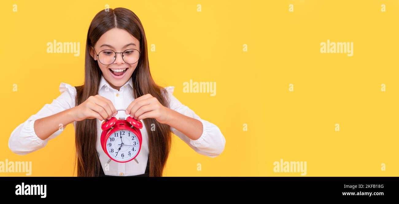 amazed child in school uniform and glasses with alarm clock showing ...