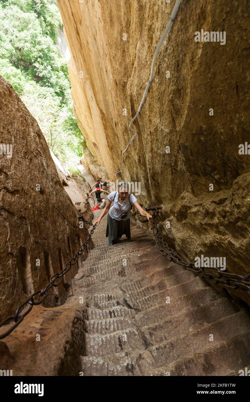 Female Western European tourist woman climbs steep steps cut and carved ...