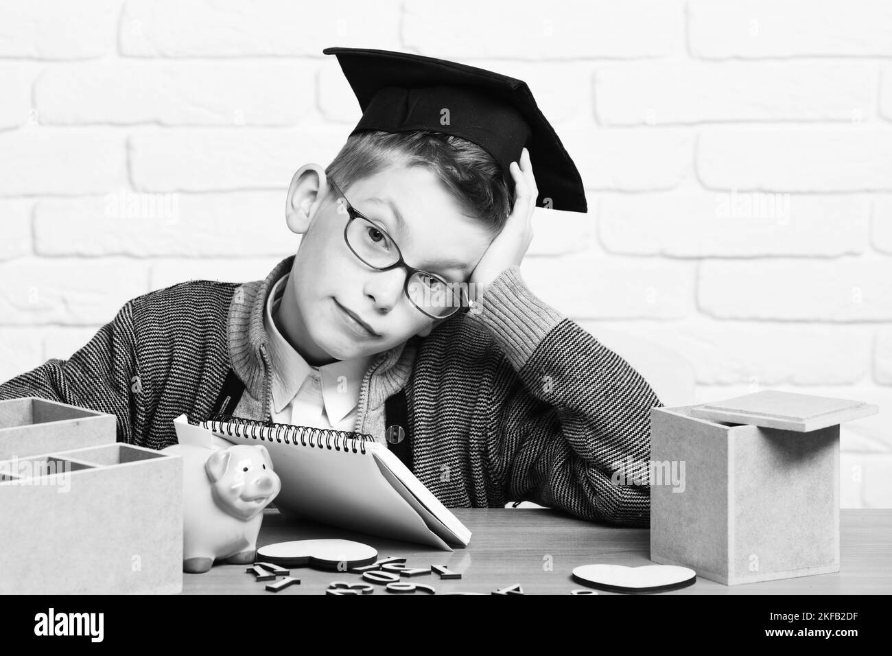 young cute pupil boy in grey sweater and glasses sitting at desk with ...