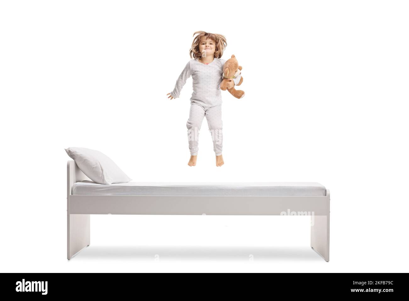 Little girl in pajamas holding a teddy bear and jumping on a bed ...