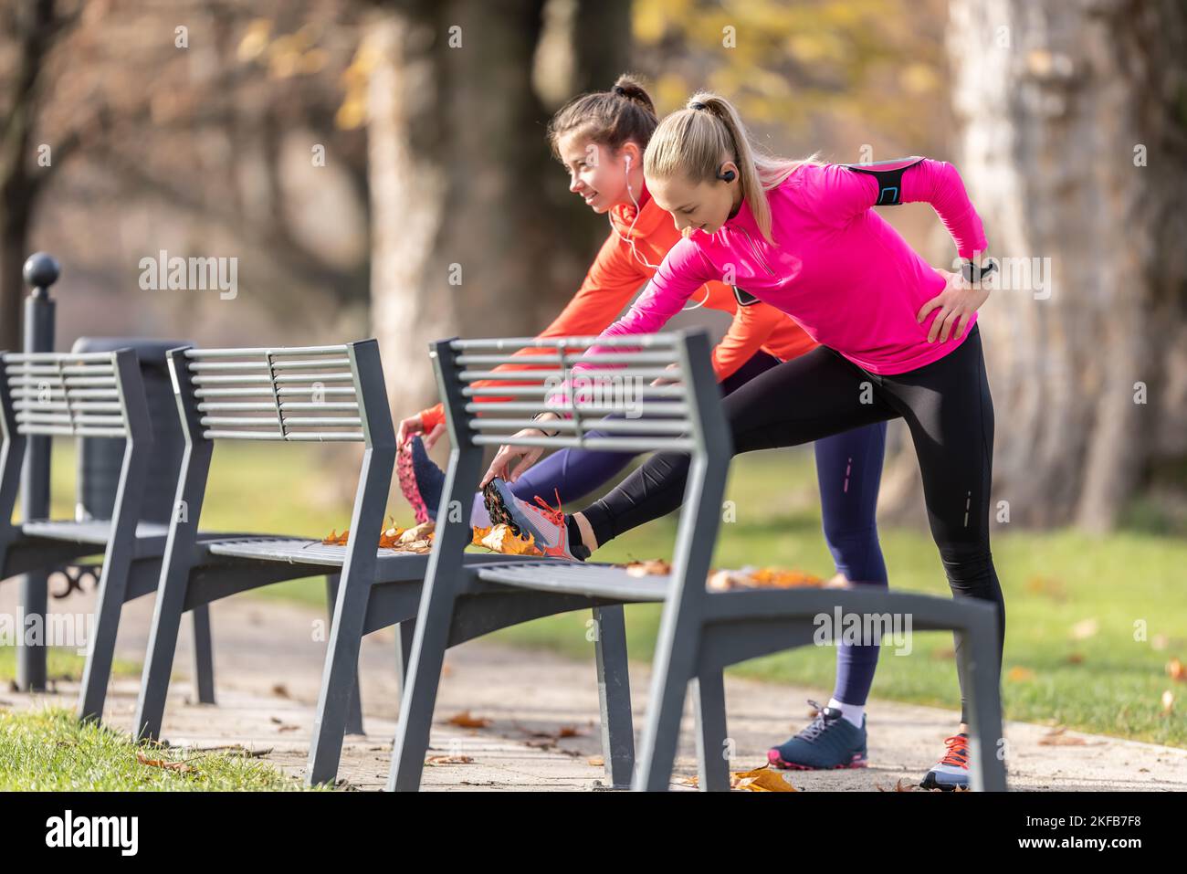 Two female athletes are warming up in the autumn park, using a bench to ...