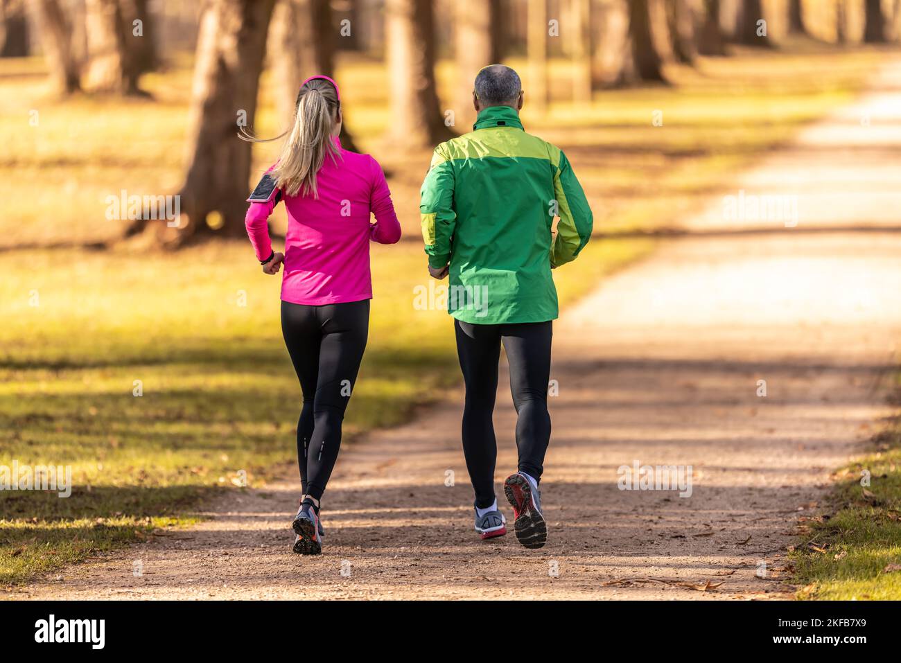 Rear view of a two runners, young woman and one mature man running in ...