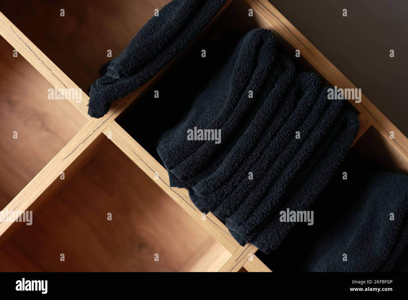 Stack of many clean black towels on two wooden shelves on white wall ...