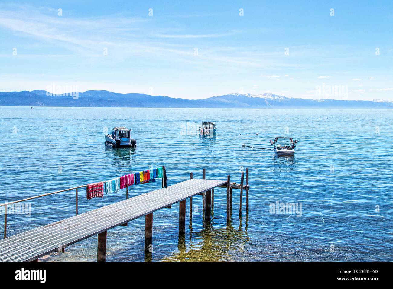 Dock with beach towels drying stretching out onto Tahoe lake with boats moored offshore and ...